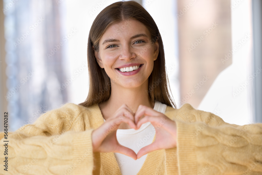 Cheerful beautiful young woman keeping finger heart at chest, showing ...