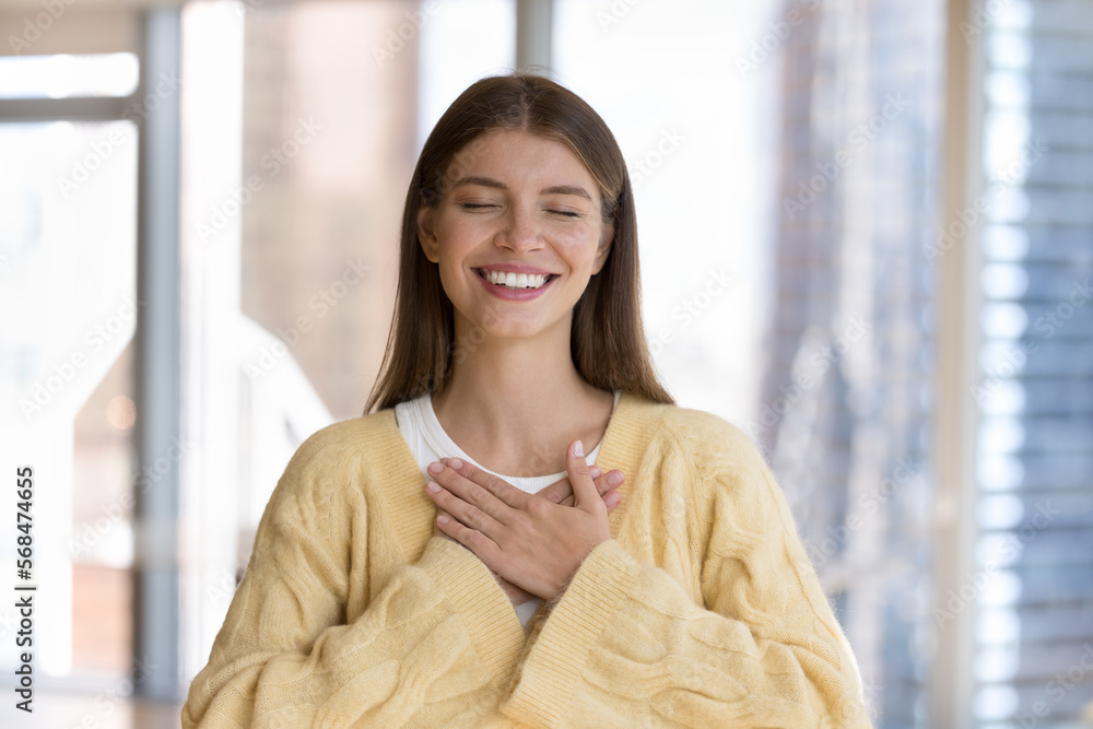 Happy pretty young woman applying hands at chest with gratitude, posing ...