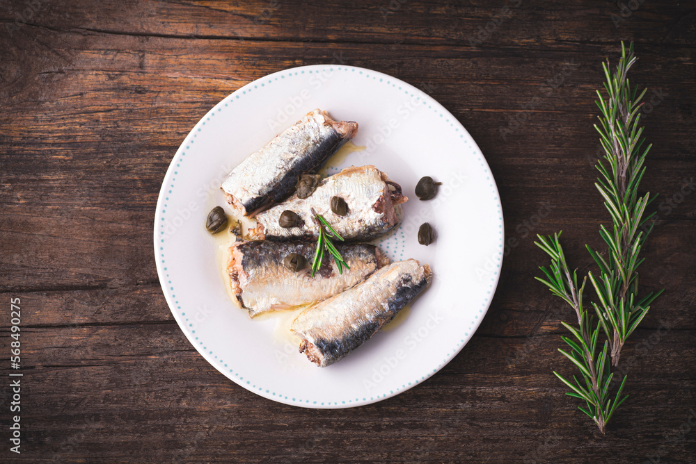 Sardines in olive oil with capers and herbs on a white plate, rustic ...