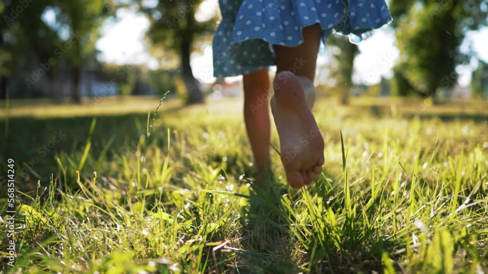 Little cheerful girl with bare feet run along green grass in nature ...
