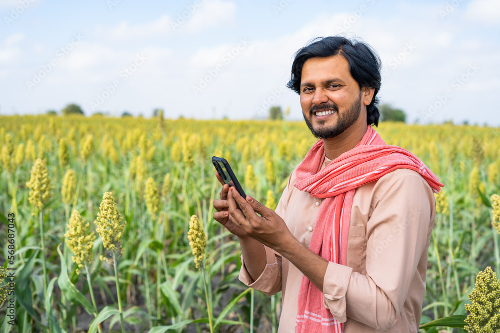 Farmer with mobile phone at agricultural farm land looking at camera ...
