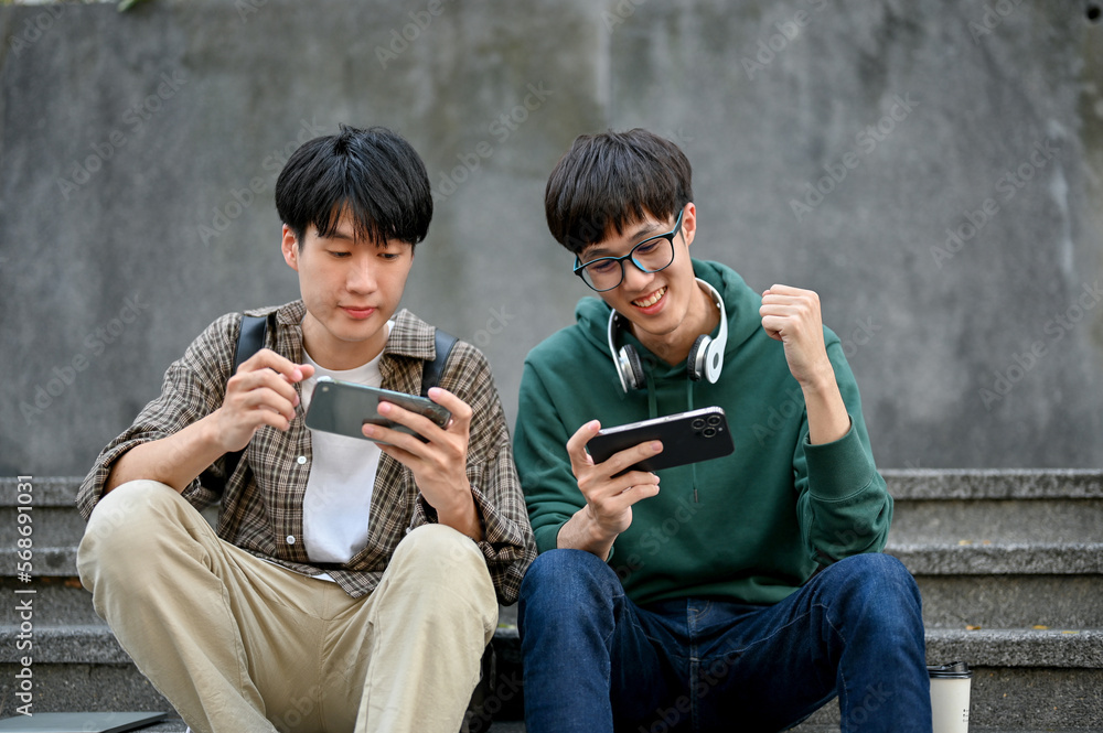 Happy Asian man college student playing mobile game on his smartphone ...