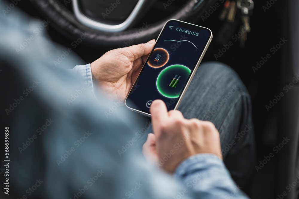 Mature woman operating electric car through mobile app on smart phone ...