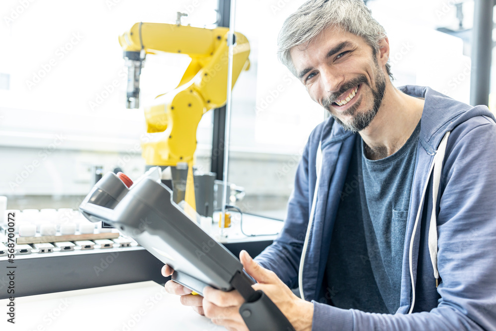 Skilled worker in robotic factory controlling robot arm with digital ...