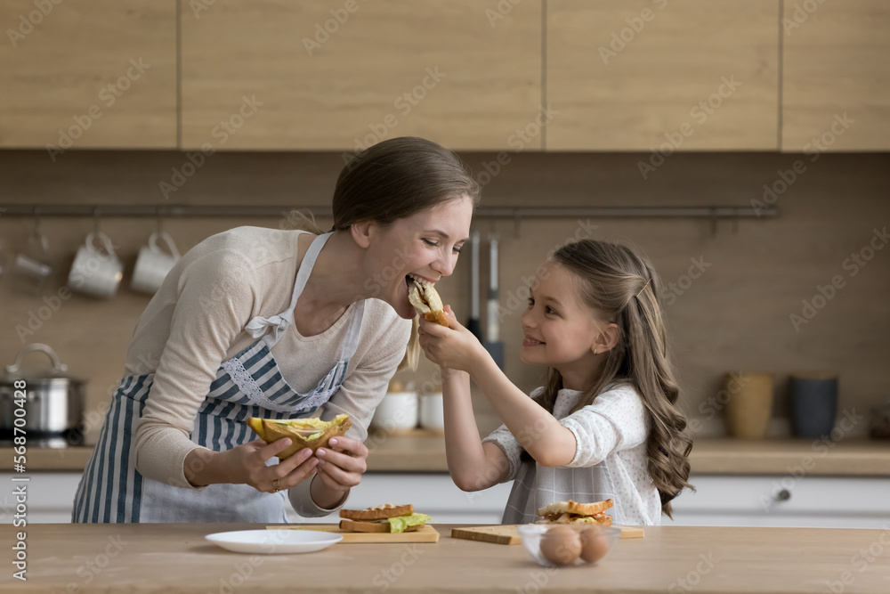 Joyful little kid girl giving mom sandwich to bite. Happy mother and ...