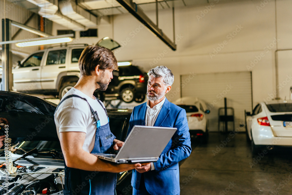 Foto Stock Handsome male mechanic wearing uniform, using laptop talking ...