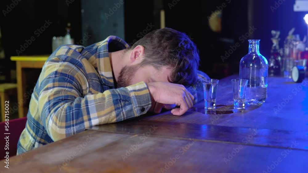 A very drunk young man is lying with his head on a table in a bar vídeo ...