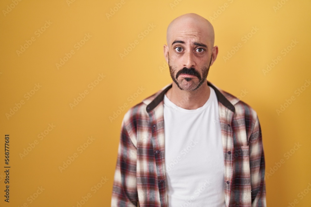Hispanic man with beard standing over yellow background depressed and ...