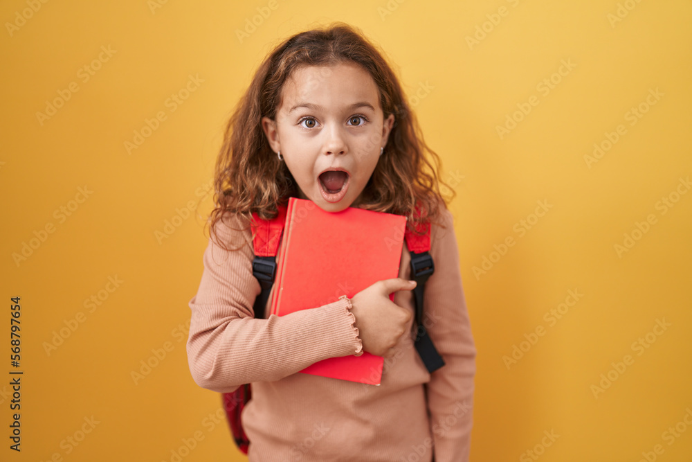 Little caucasian girl wearing student backpack and holding book scared ...