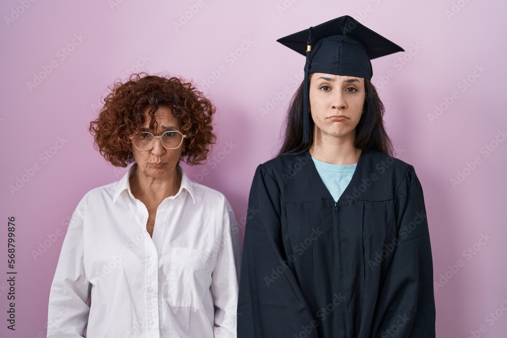 Hispanic mother and daughter wearing graduation cap and ceremony robe ...