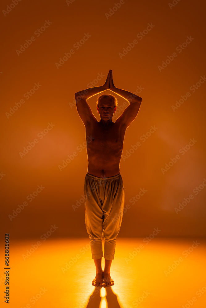 full length of shirtless man in pants standing in warrior pose on ...