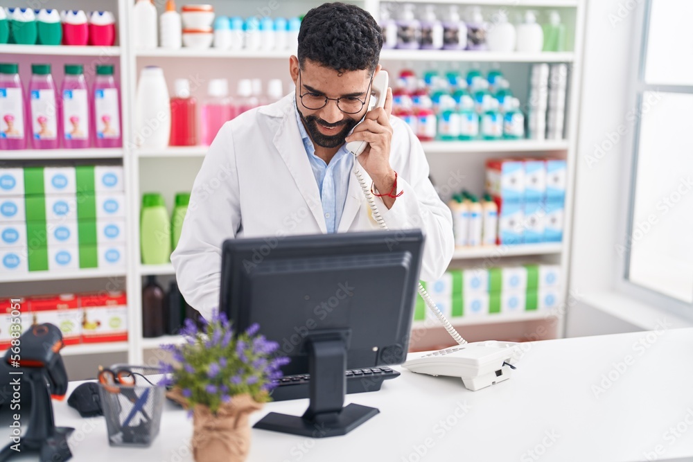 Young arab man pharmacist talking on telephone using computer at ...