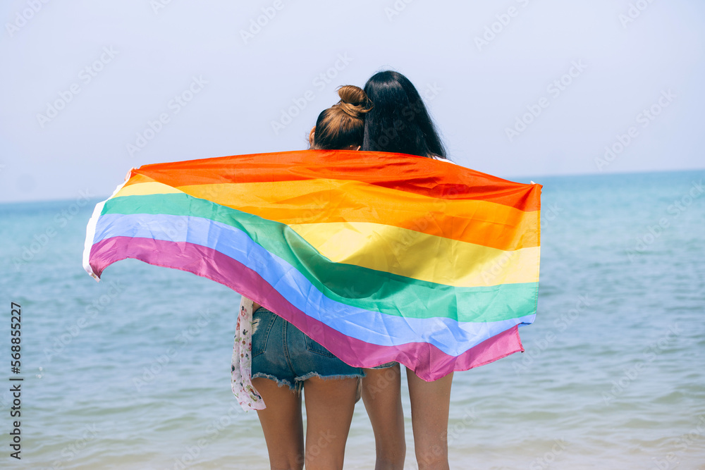 LGBTQI couple on the beach with rainbow flag beautiful female young ...