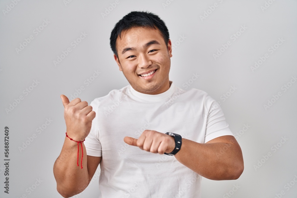 Young chinese man standing over white background pointing to the back ...