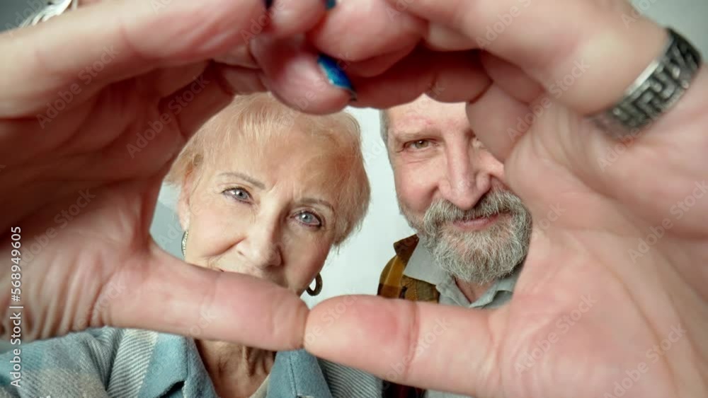 Portrait of a happy elderly couple is making hand heart, looking at ...