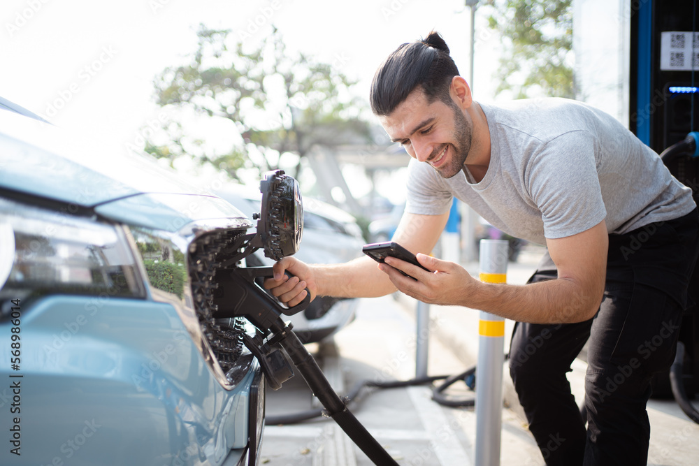 Handsome Asian young man holding an EV plug connector and attaching ...