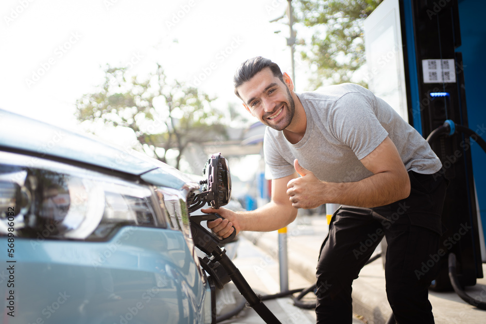 Handsome Asian young man holding an EV plug connector and attaching ...