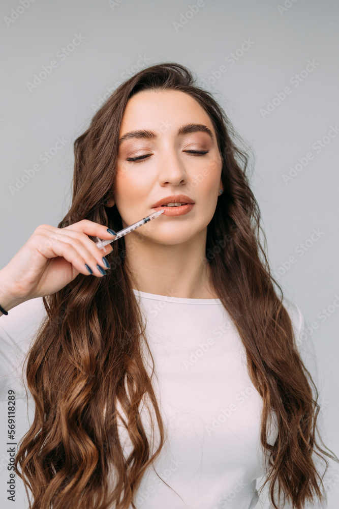 young girl beautician makes an injection of hyaluronic acid into her ...