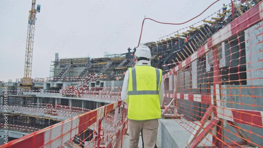 Engineer with color safety vest and hardhat walks along concrete ...