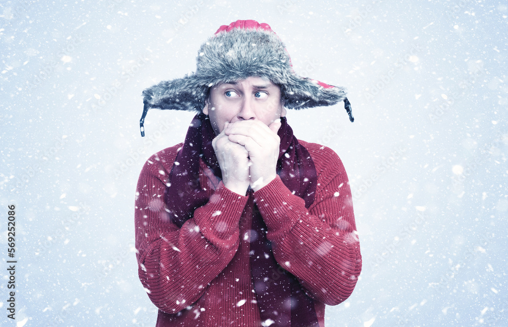 Frozen man in a red sweater, scarf and hat stands warming his hands on ...