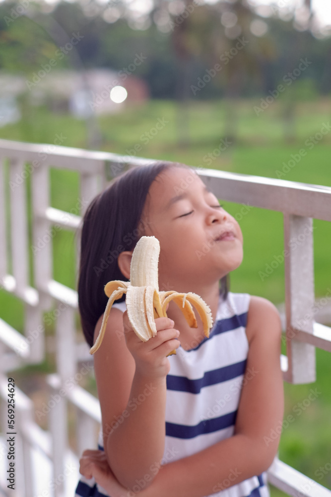Portrait of cute little asian girl eat banana with nature background ...