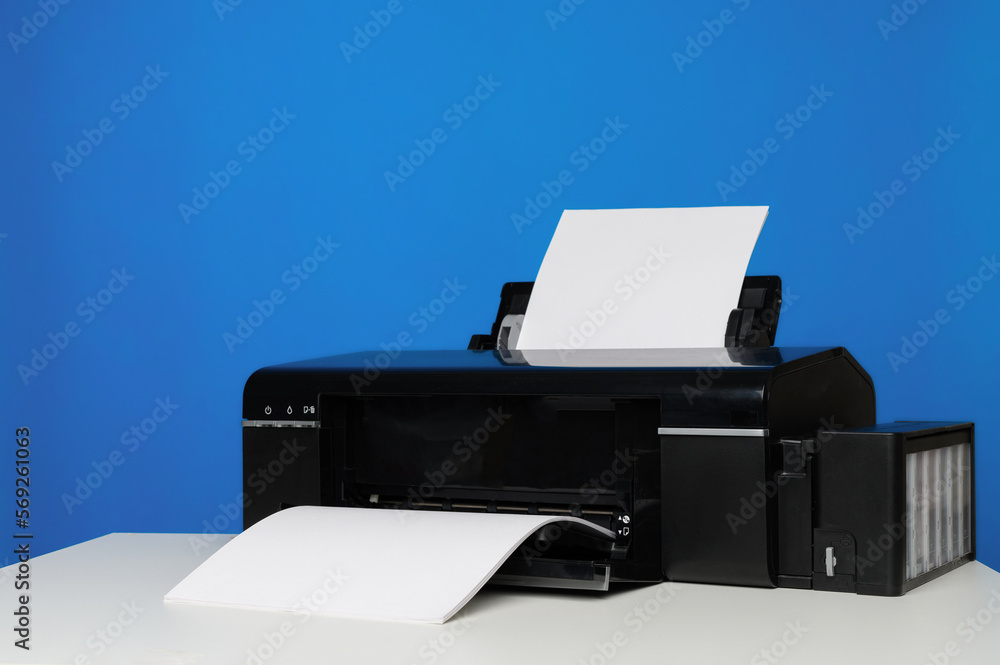 Front view of a printer and a blank sheet of A4 paper on a blue ...