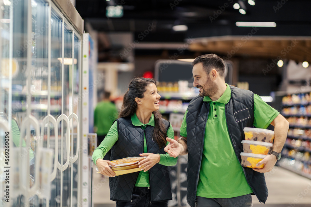 Happy supermarket workers are chatting and carrying groceries to ...