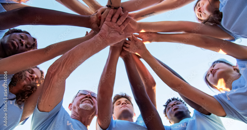 Cheerful group of volunteers looking at camera and stacking hands up to ...
