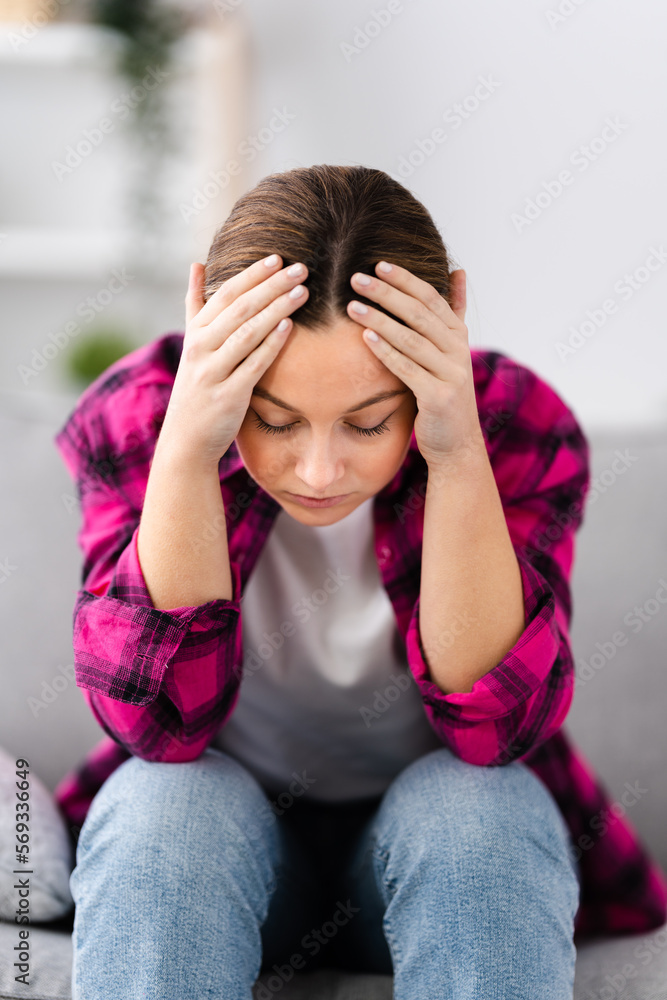 Sad young woman hands on head looking down while sitting on sofa ...