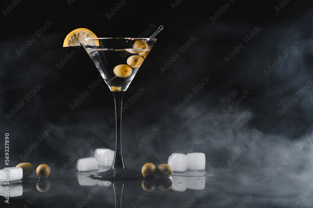 Glass of classic dry martini cocktail with olives on dark table against ...