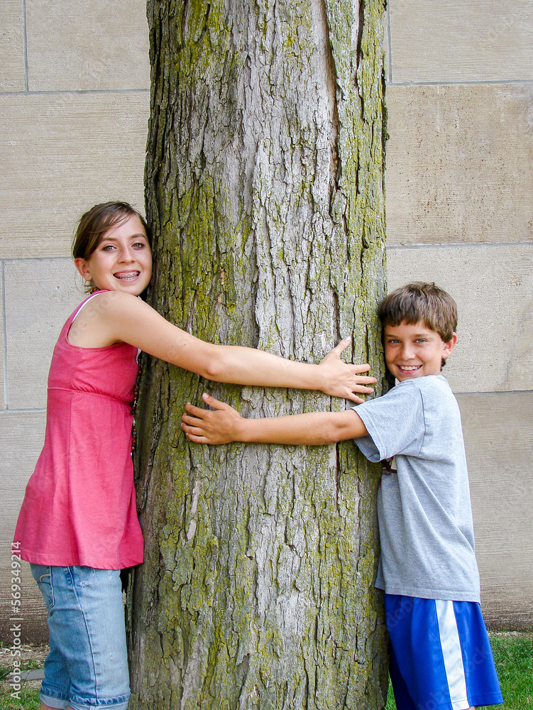 Two children hugging a tree in an urban setting. Stock Photo | Adobe Stock