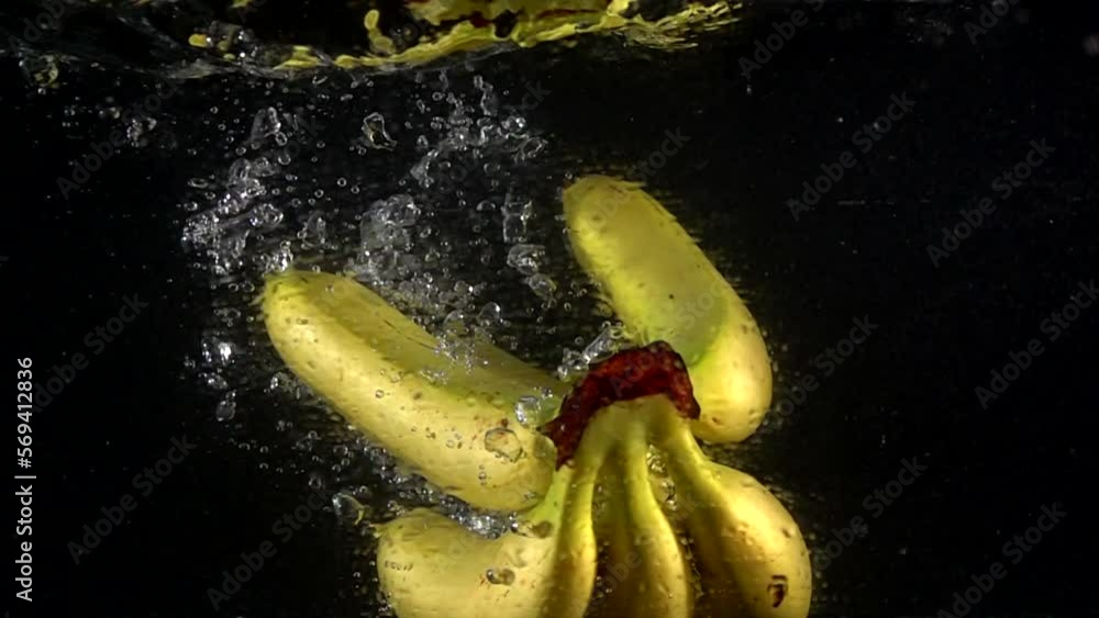 Super slow motion fresh bananas fall into the water with splashes. On a ...