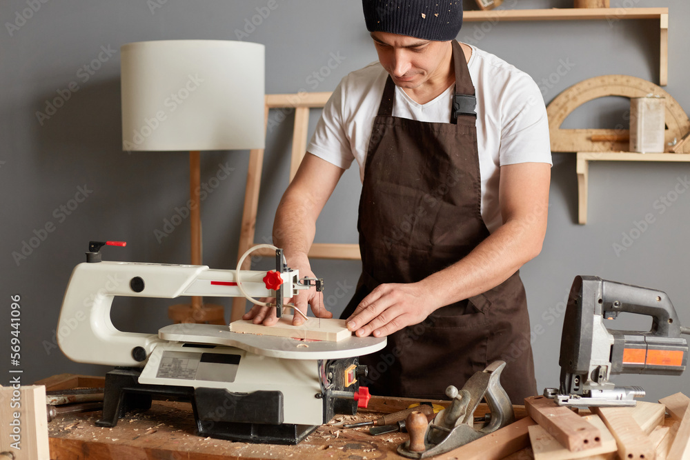 Horizontal shot of concentrated man carpenter wearing brown apron and ...
