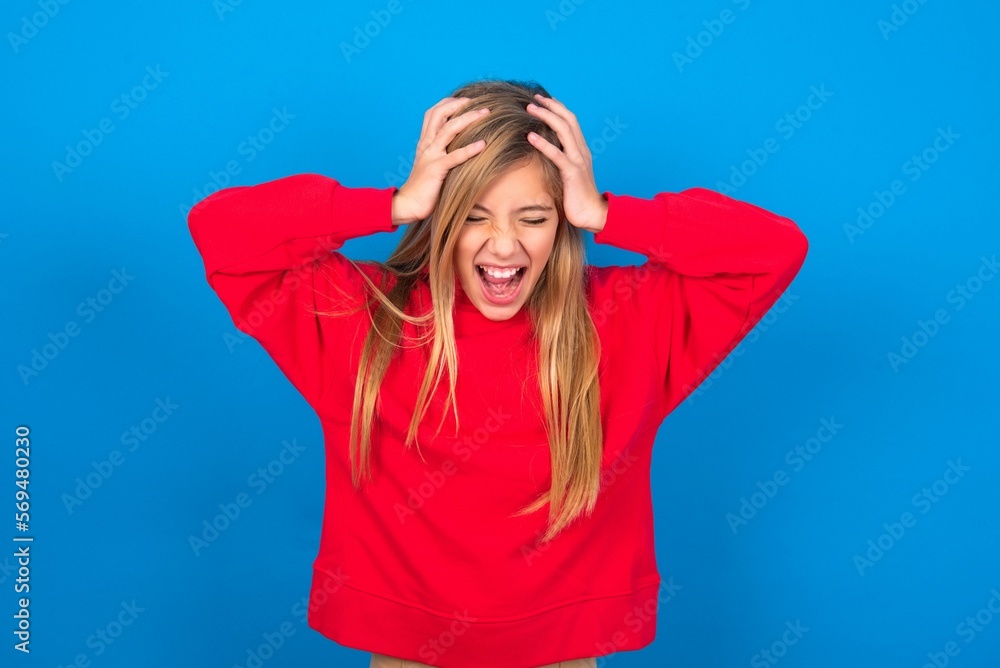 Shocked panic caucasian teen girl wearing red sweater over blue studio ...