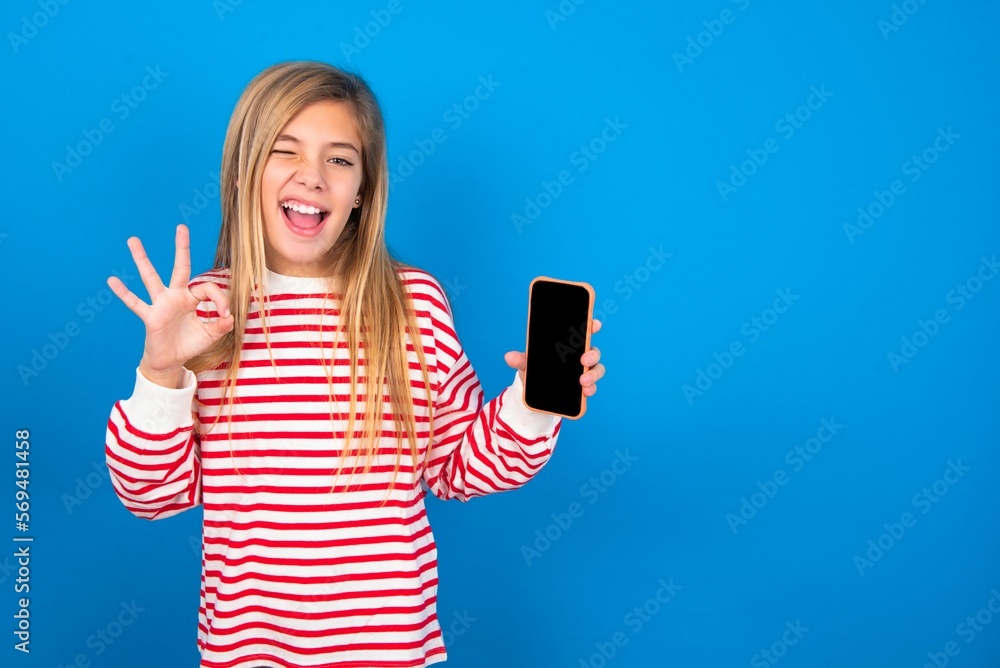Excited caucasian teen girl wearing striped shirt over blue studio ...