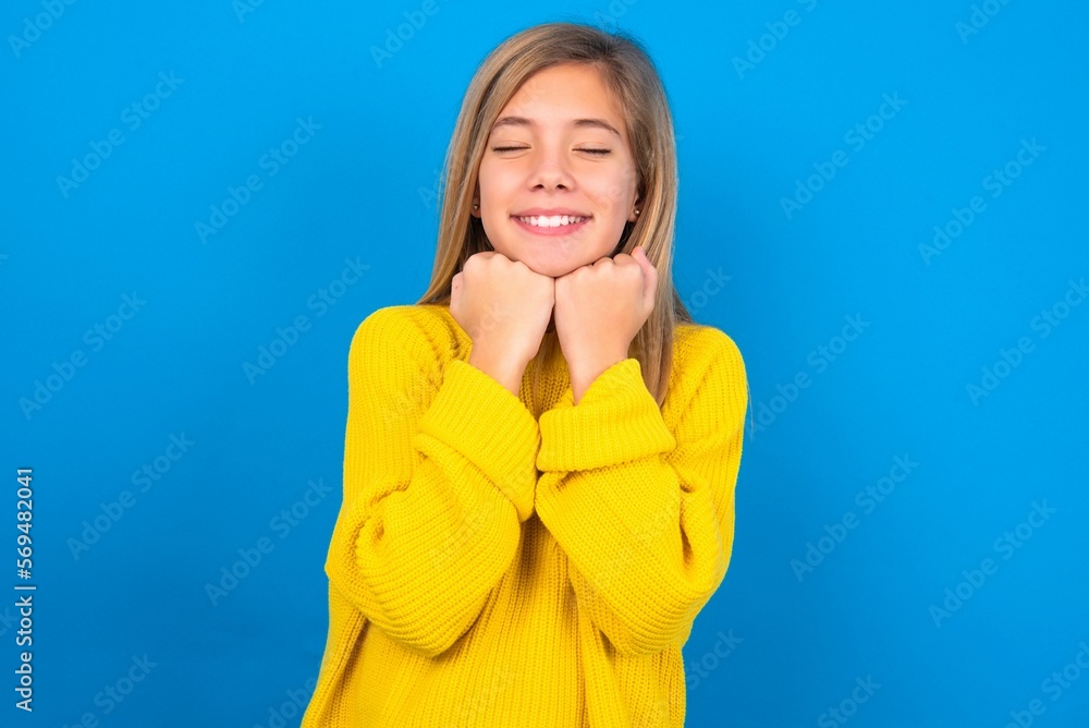 Cheerful caucasian teen girl wearing yellow sweater over blue studio ...