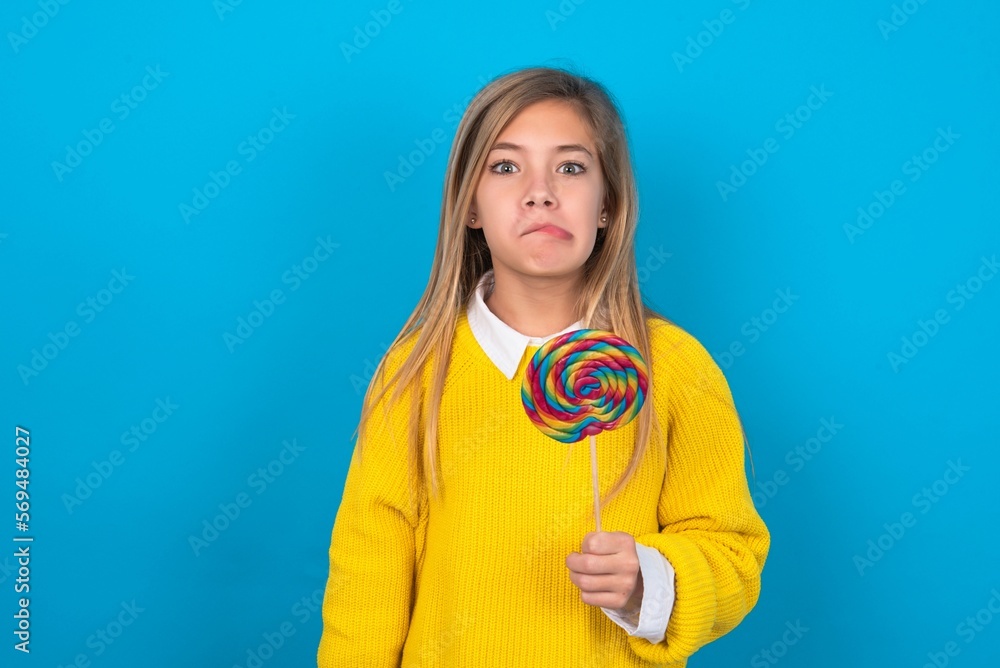 caucasian teen girl wearing yellow sweater over blue studio background ...