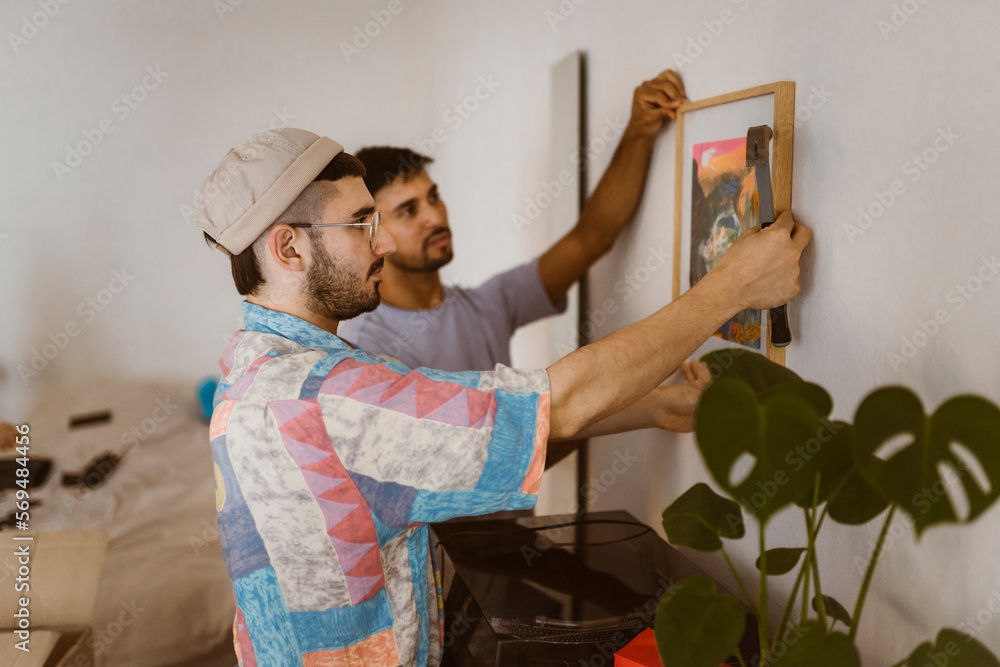 Side view of man hanging frame on wall with boyfriend at home Stock ...