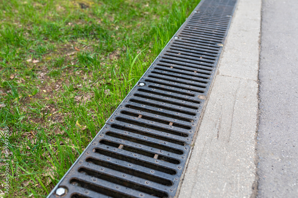 A rusted metal sewer grate along a paved walkway. The edge of the ...