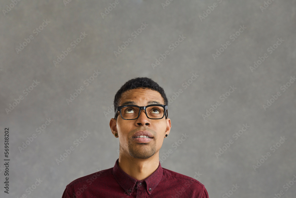 Dark-skinned man with doubtful facial expression looking up on gray ...