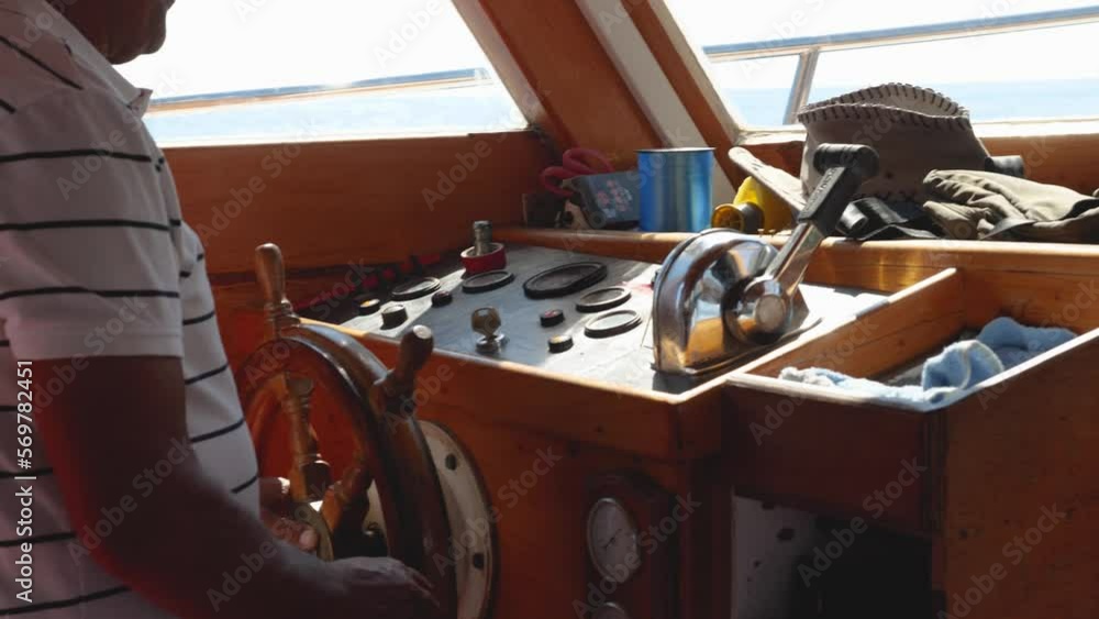 A captain is turning a wooden wheel on a ship. The boat is sailing on ...