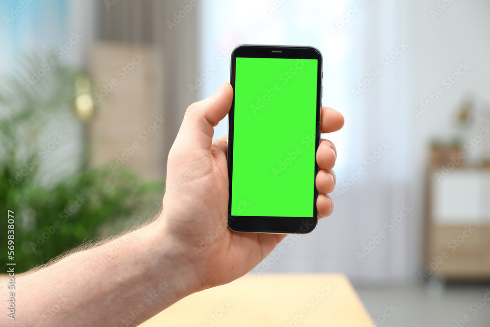 Man holding smartphone with green screen indoors, closeup. Gadget ...