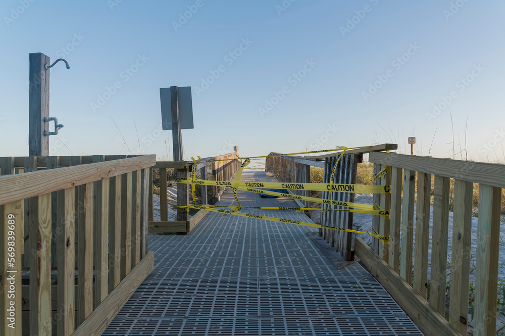 Closed part of a boardwalk with yellow caution tape tied on the wooden ...