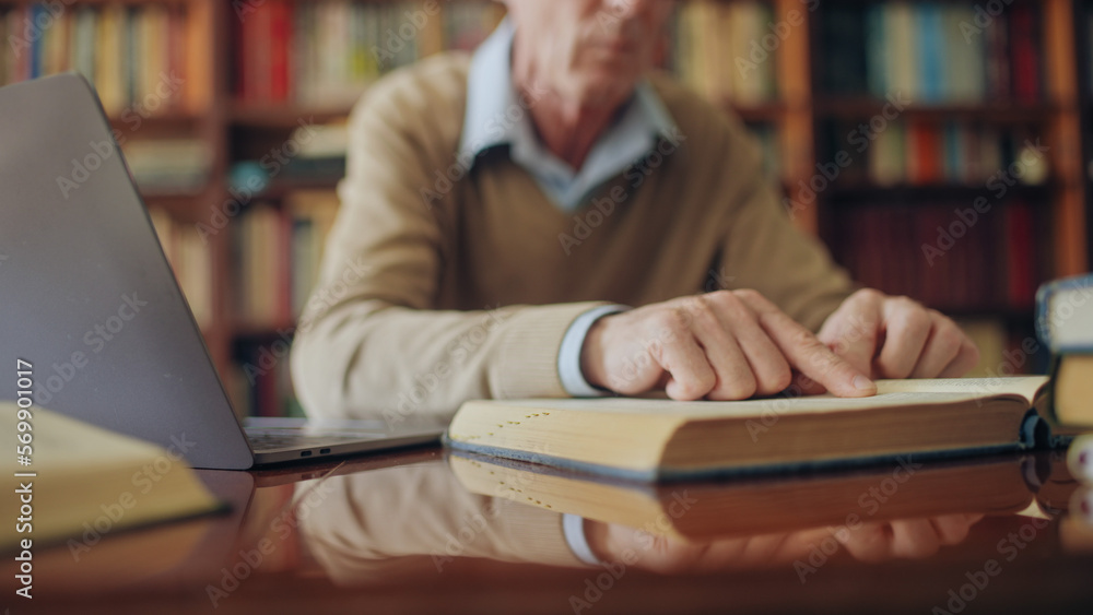 Senior historian reading a book and typing notes on laptop, working on ...
