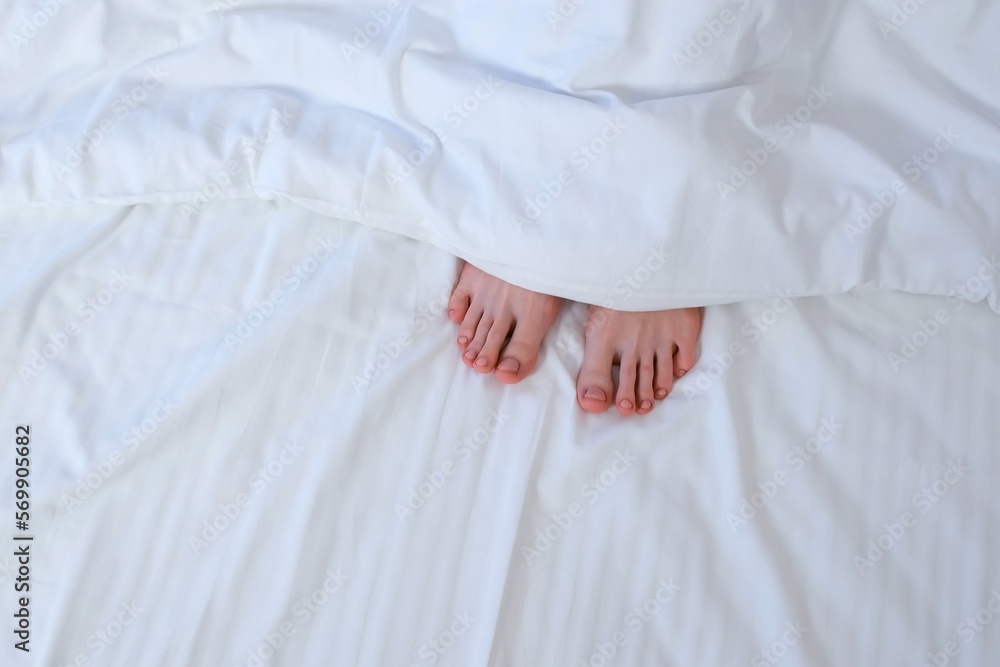 Woman's moving feet hiding it under blanket in bed among white linen ...