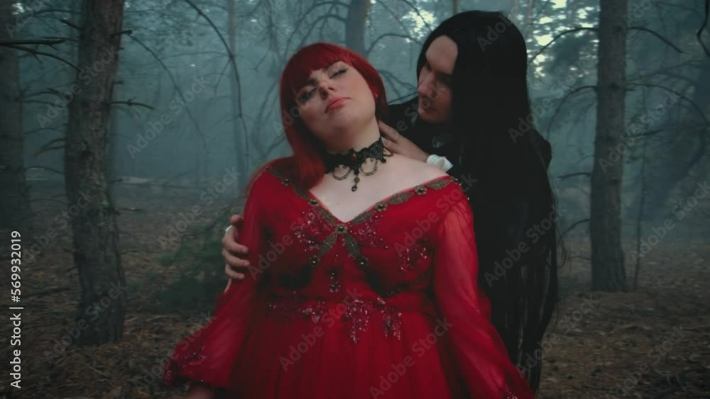 Goth man vampire in black tailcoat hugs bites kisses neck drinks blood ...