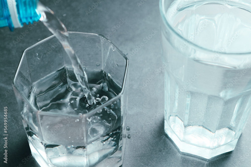 Pouring water from bottle into glass on grey background. Refreshing ...