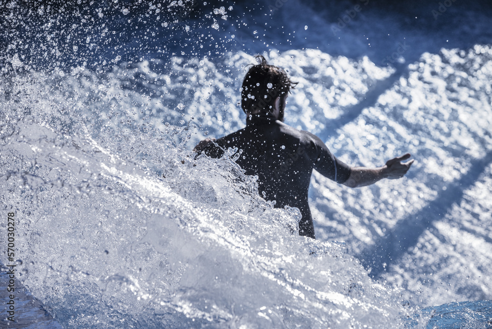 A surfer giving it a go in a wave pool with big splashes in the turns ...