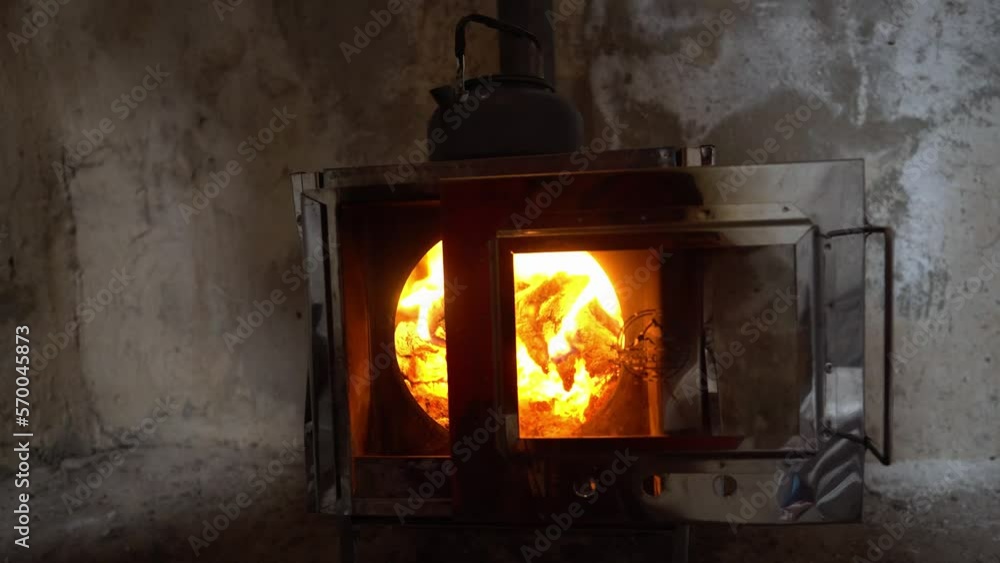A kettle is boiling on a camp stove with fire. Water is pouring out ...