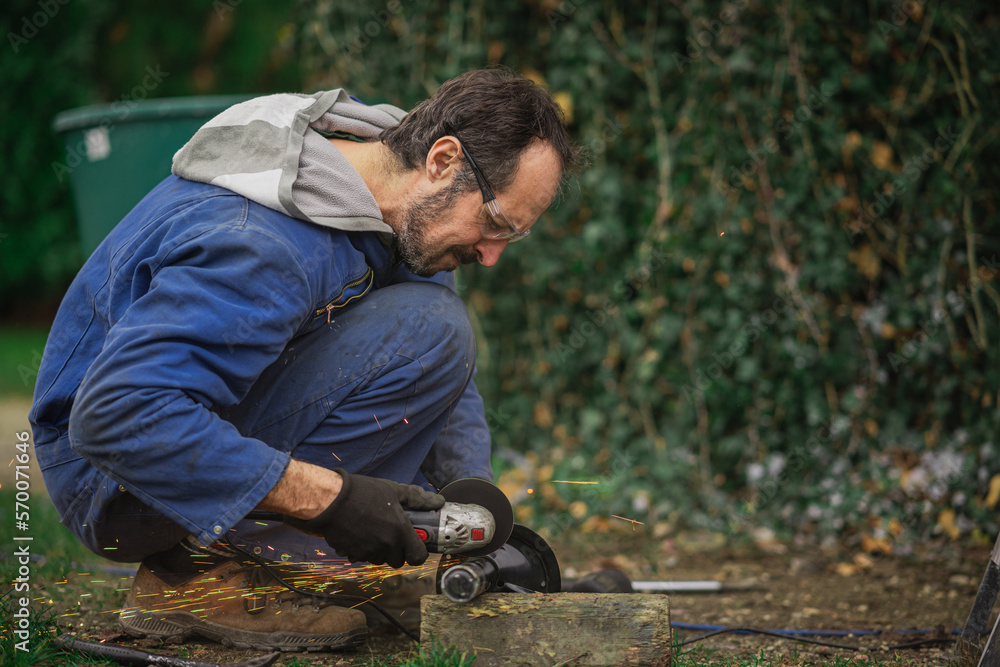 Man in blue overalls is using an angle grinder to cut away parts of ...